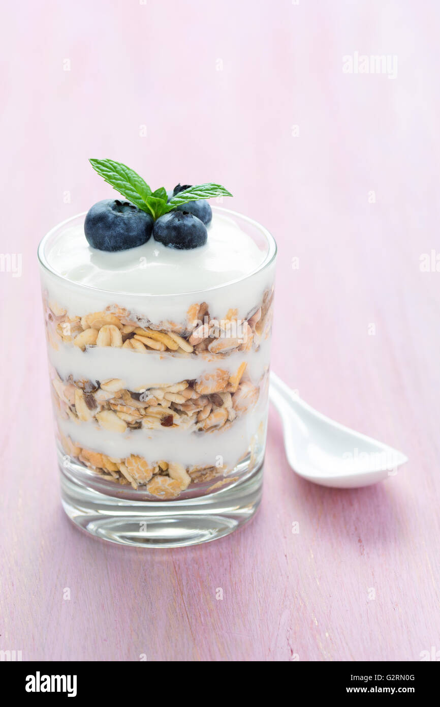 A glass of layered yoghurt, cereals, blueberry and mint on a pink ...
