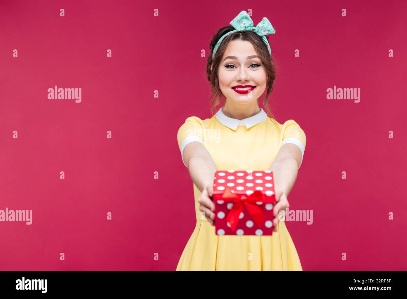 Smiling beautiful young woman giving you a present in box over pink ...
