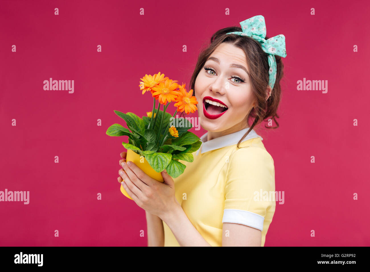 Portrait of charming cheerful pinup girl woth orange flower in pot over ...