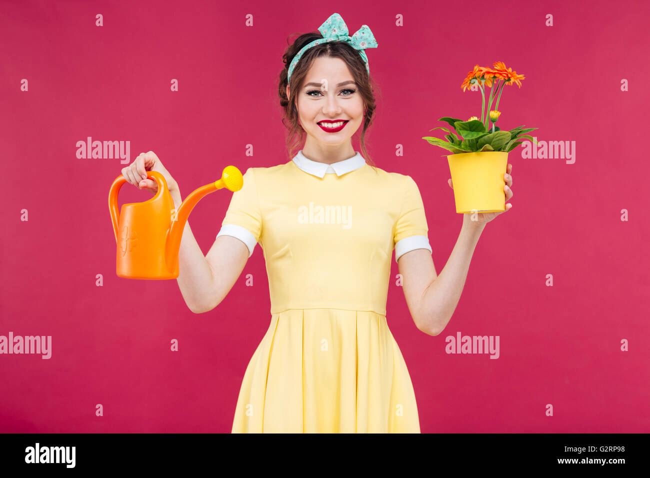 Smiling lovely pinup girl holding flowers in pot and orange watering ...