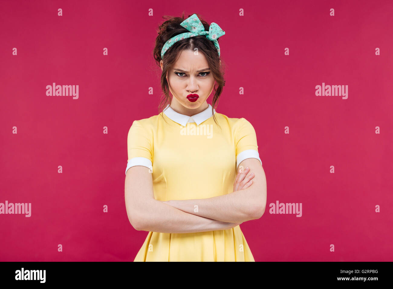 Sad frowning pinup girl in yellow dress standing with arms crossed over ...