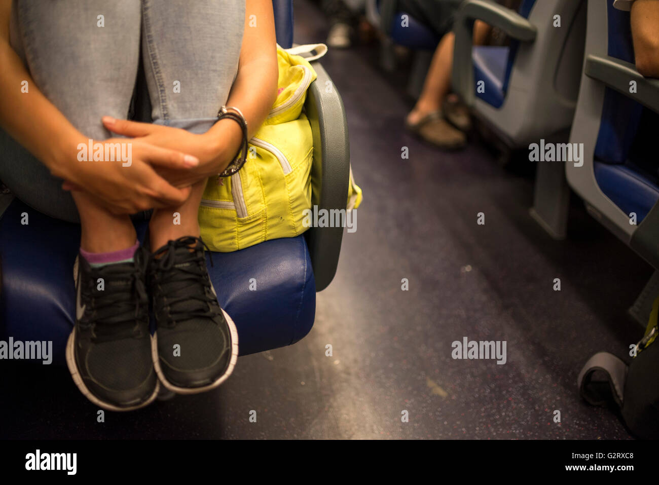 A young woman embracing her legs in the seat of a train as it moves ...