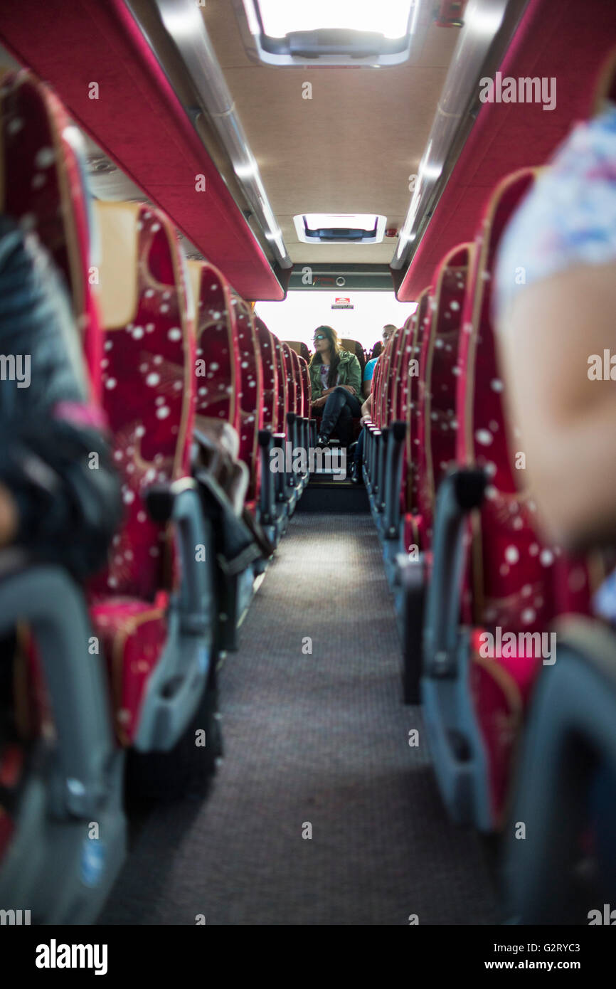 The corridor of a moving red seated turist bus mid-full of students ...