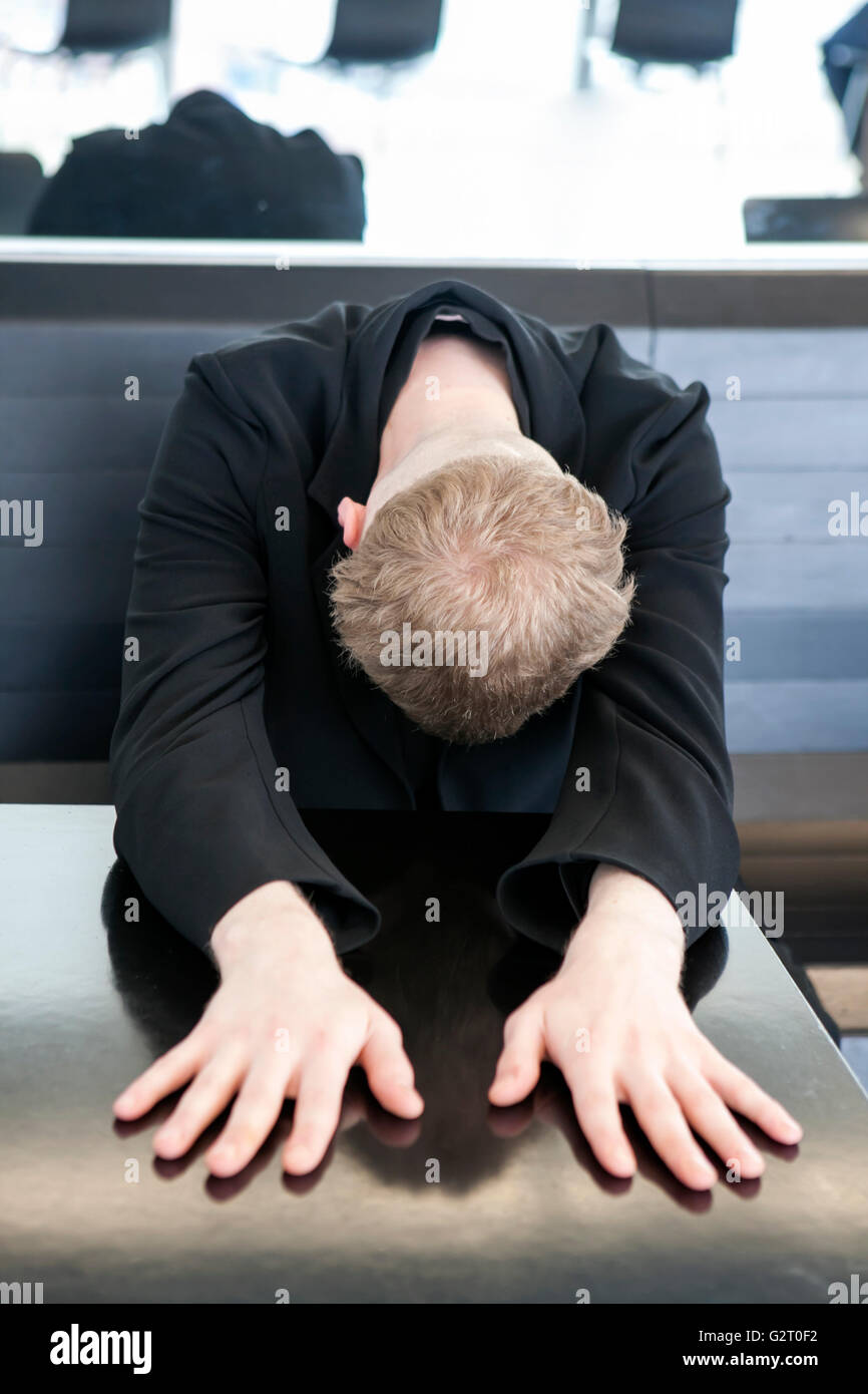 blond boy in black coat sitting at the table put his head and hands on ...