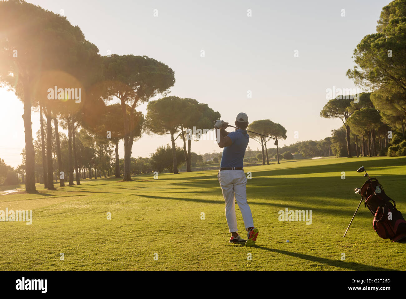 handsome sporty man, golf player hitting shot with club on course at ...