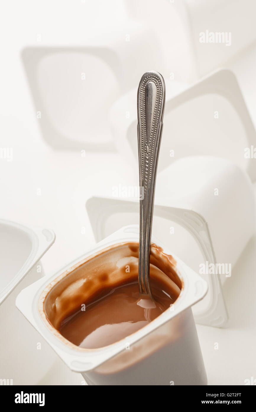 Open yogurt in pot with metal spoon and empty plastic yogurt pots Stock ...