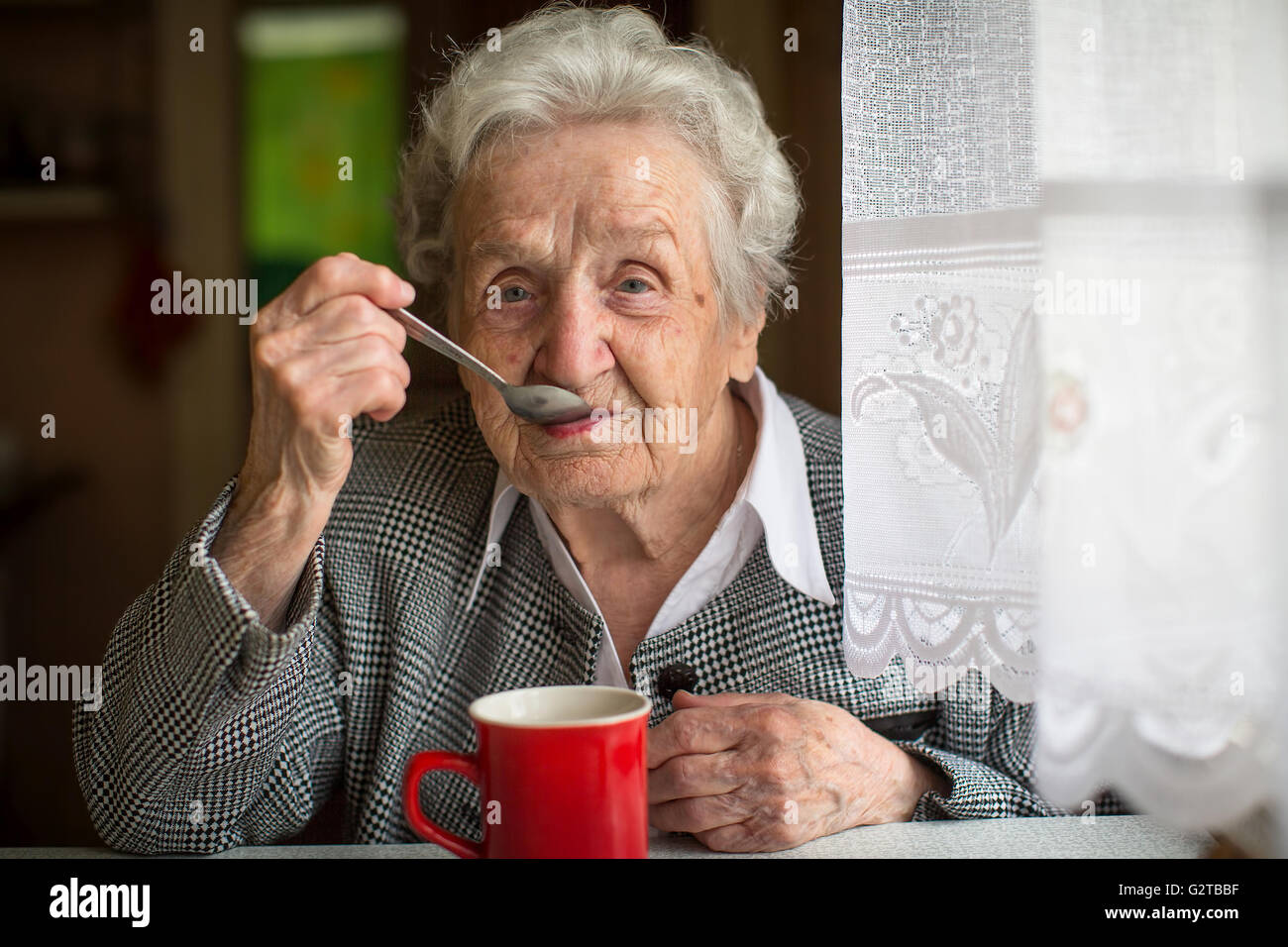 Elderly woman drinking tea sitting in the kitchen Stock Photo - Alamy