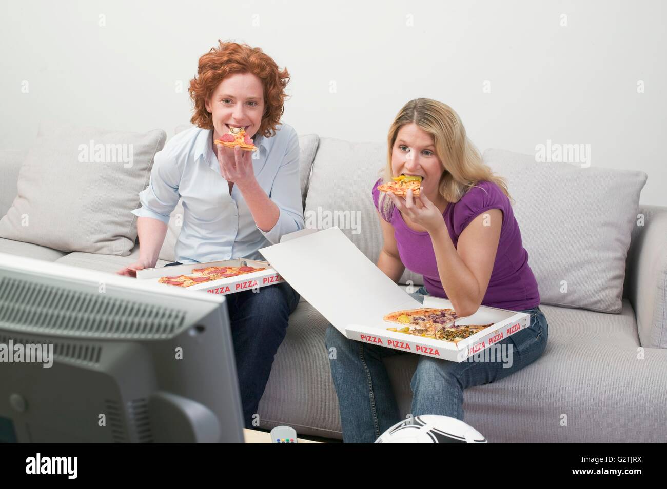 Two friends eating pizza while watching TV Stock Photo - Alamy