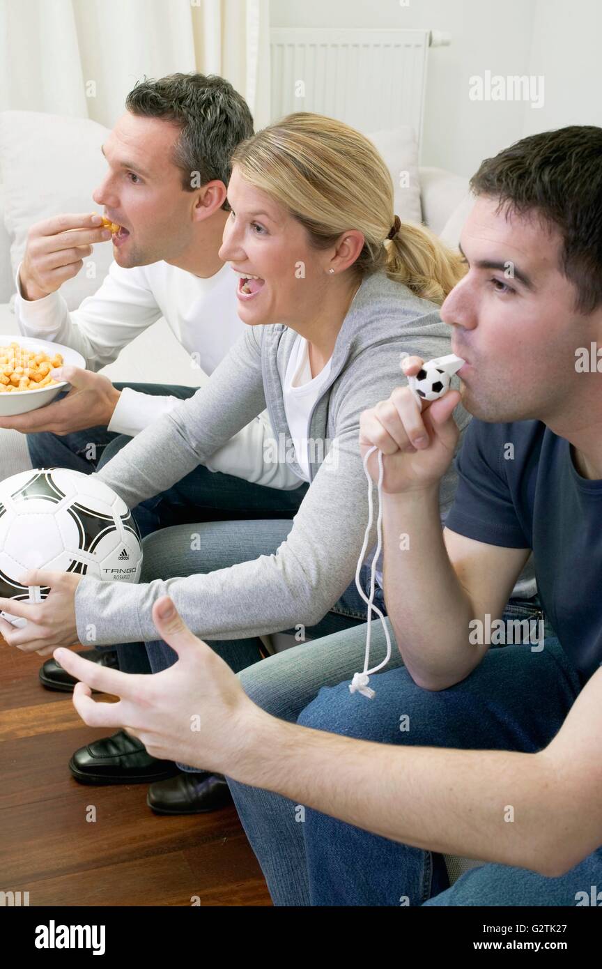 Friends watching TV with referee's whistle, football & crisps Stock ...
