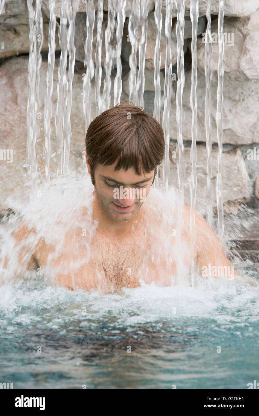 Young man standing under a waterfall Stock Photo - Alamy