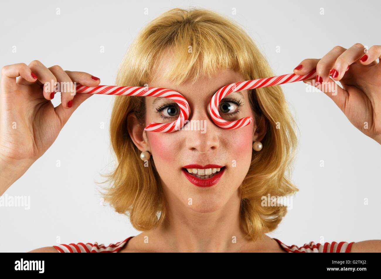 Blond woman holding candy canes in front of her eyes Stock Photo - Alamy