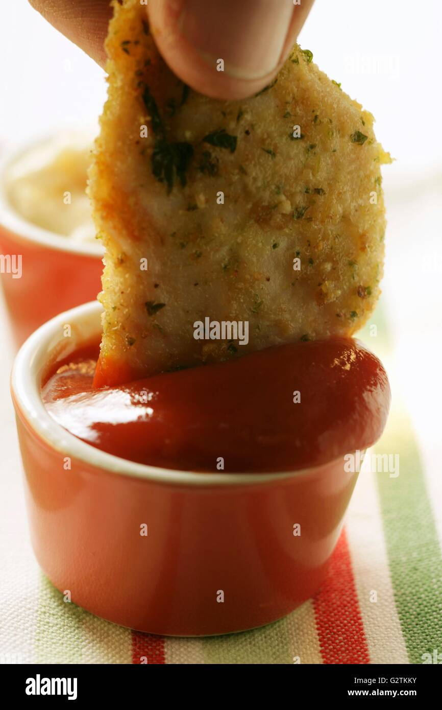 Dipping chicken nugget into ketchup Stock Photo - Alamy