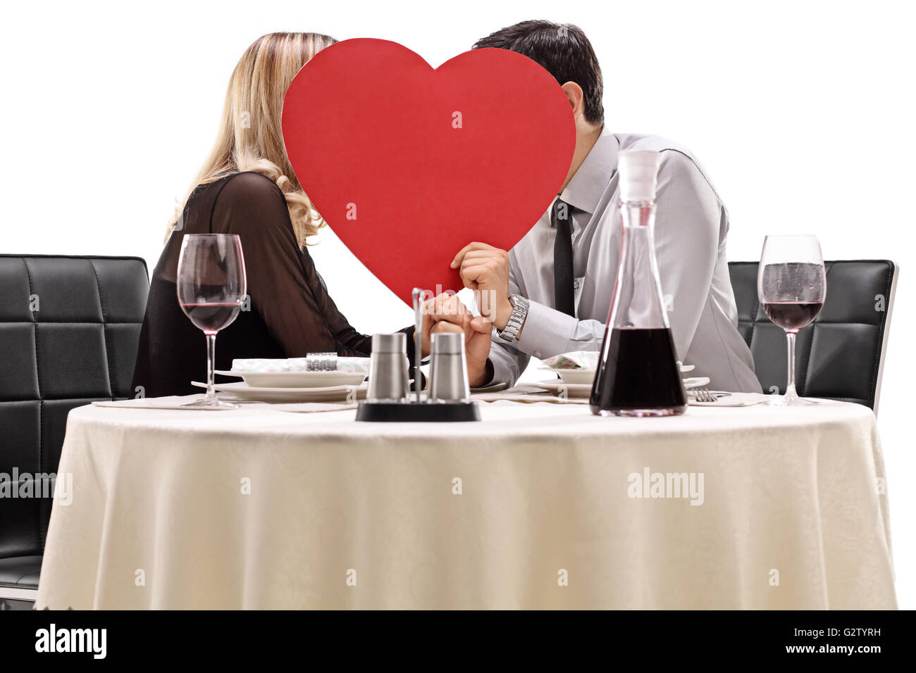 Affectionate couple sitting at a dinner table and kissing behind a red ...