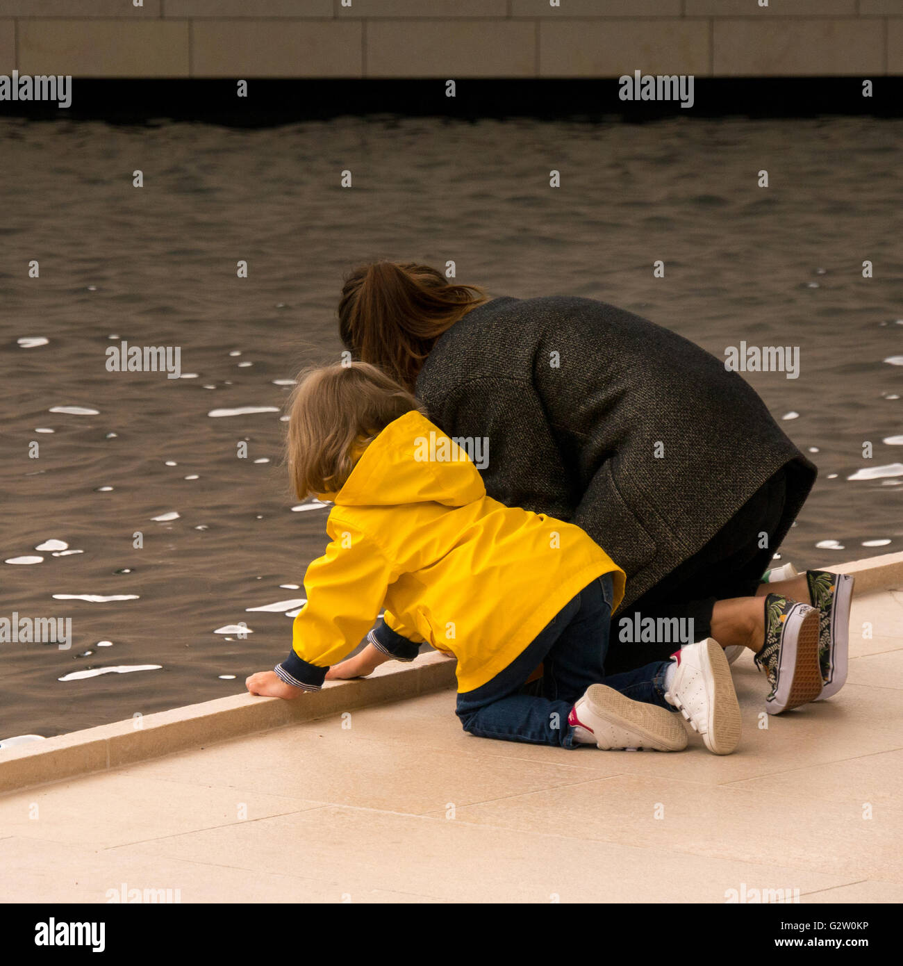 A woman and her daughter kneeling down and looking into an urban pond ...