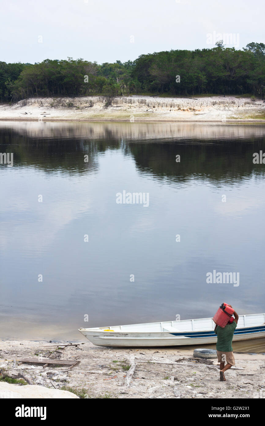 Old wooden boat moored to Amazon river shore in Brazil while one man ...