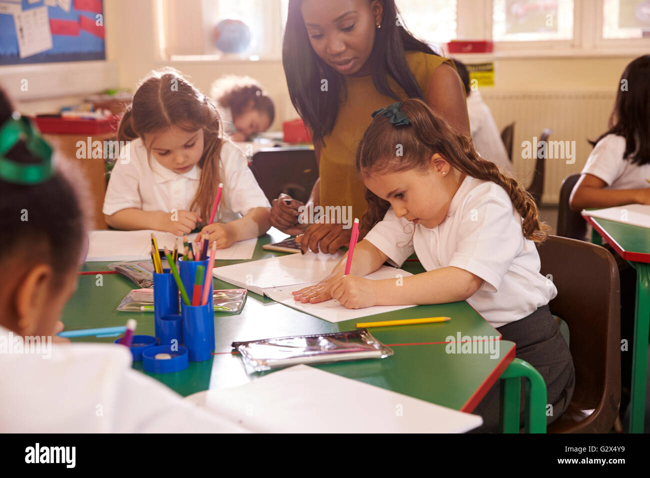 Female Elementary School Teacher Helping Pupils At Desk Stock Photo - Alamy