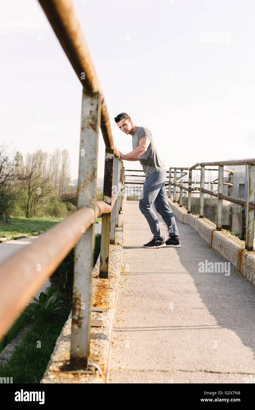 Runner man doing stretching leaning against the railing of a bridge ...