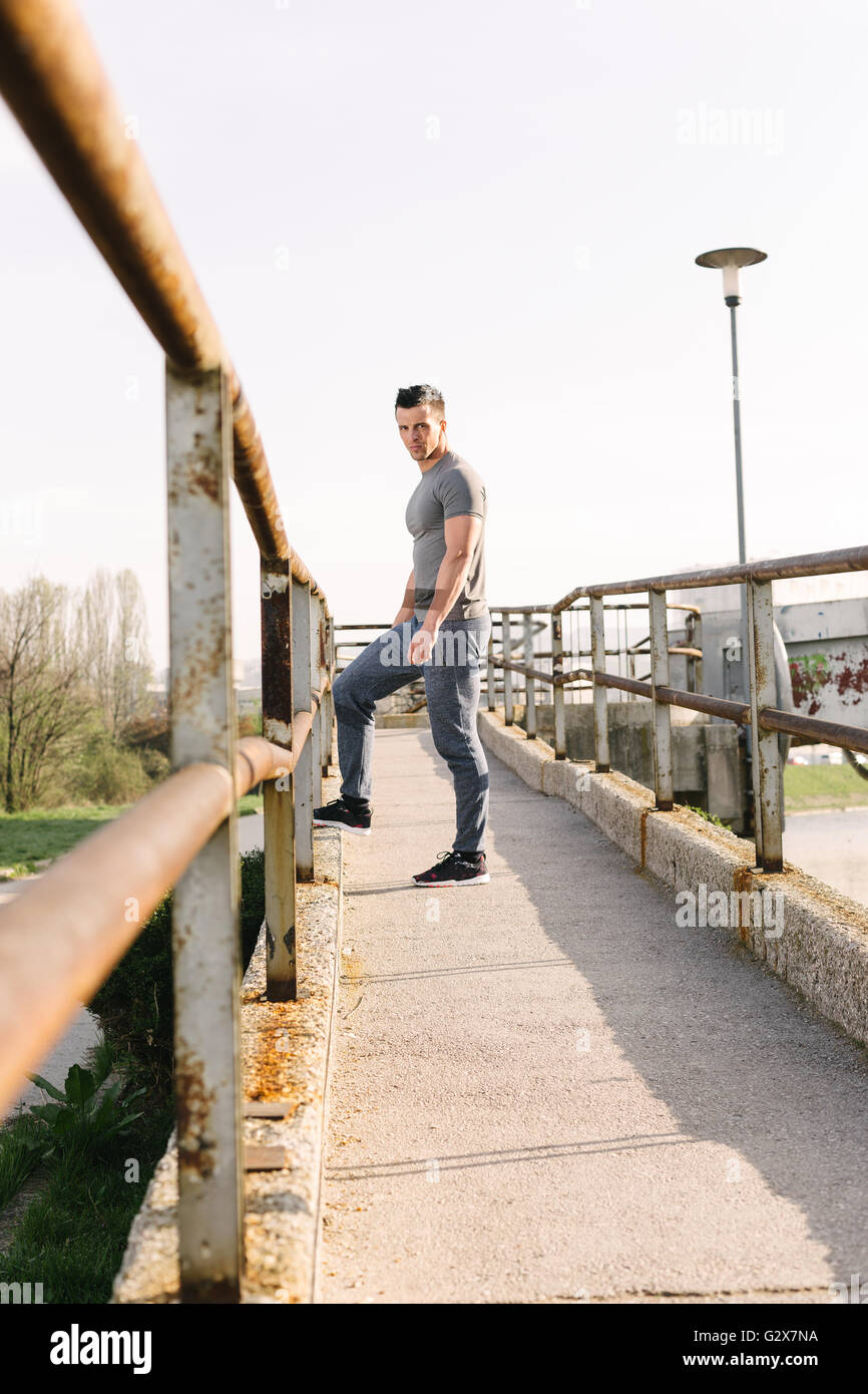 Runner man doing stretching leaning against the railing of a bridge ...