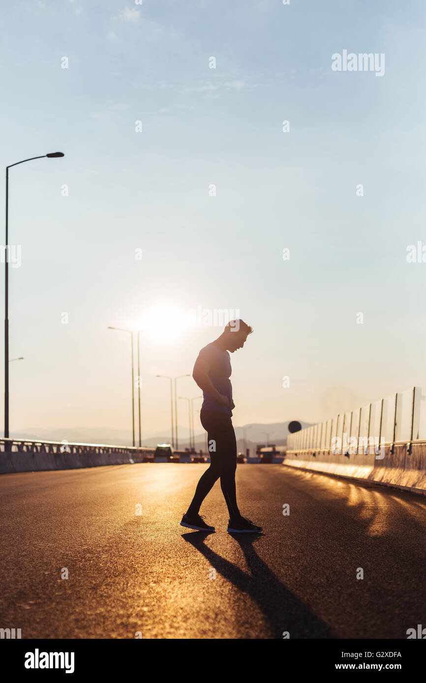 Attractive fit man running along big modern bridge at sunset light ...