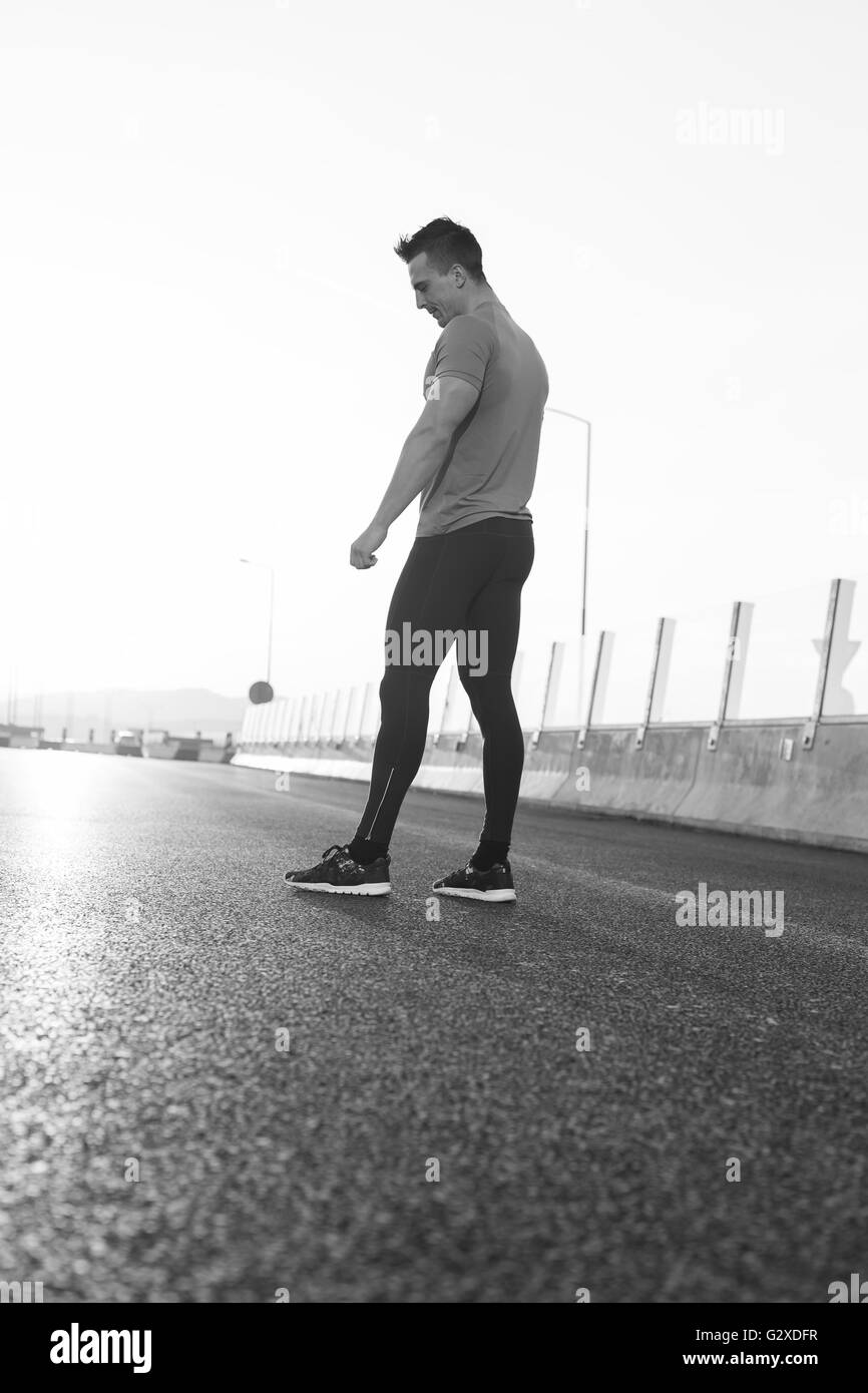Attractive fit man running fast along big modern bridge at sunset light ...
