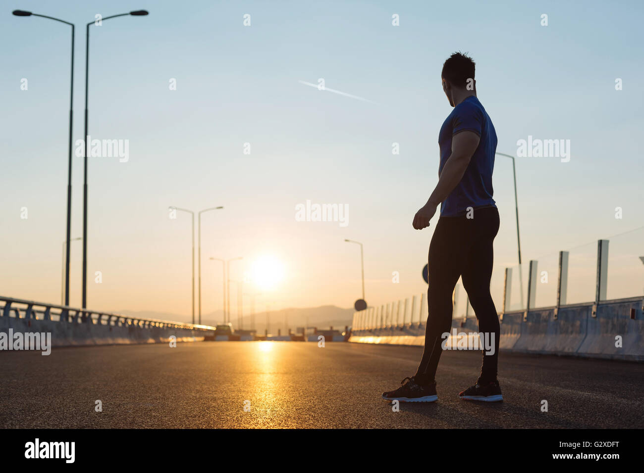 Attractive fit man running fast along big modern bridge at sunset light ...