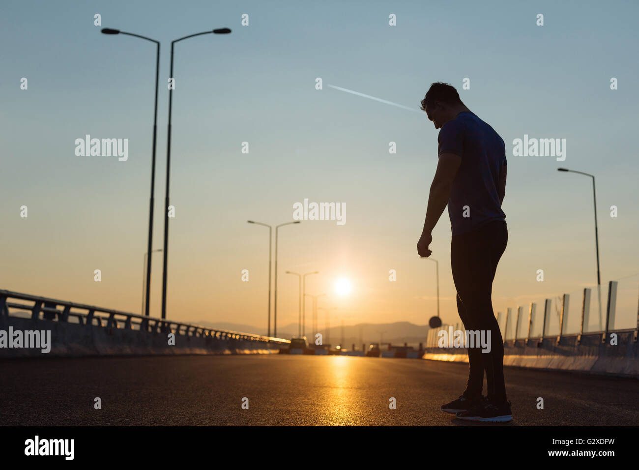 Attractive fit man running fast along big modern bridge at sunset light ...