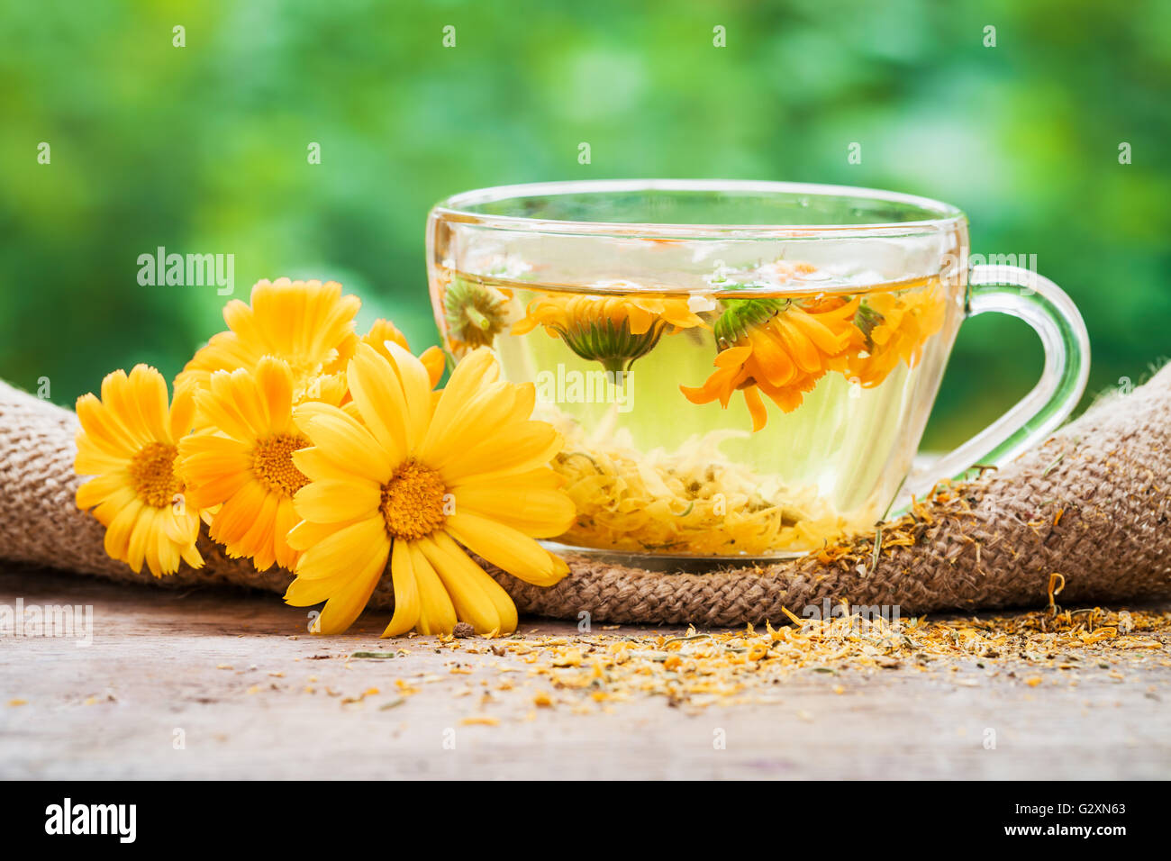 Cup of marigold tea and calendula flowers outdoors on green background ...