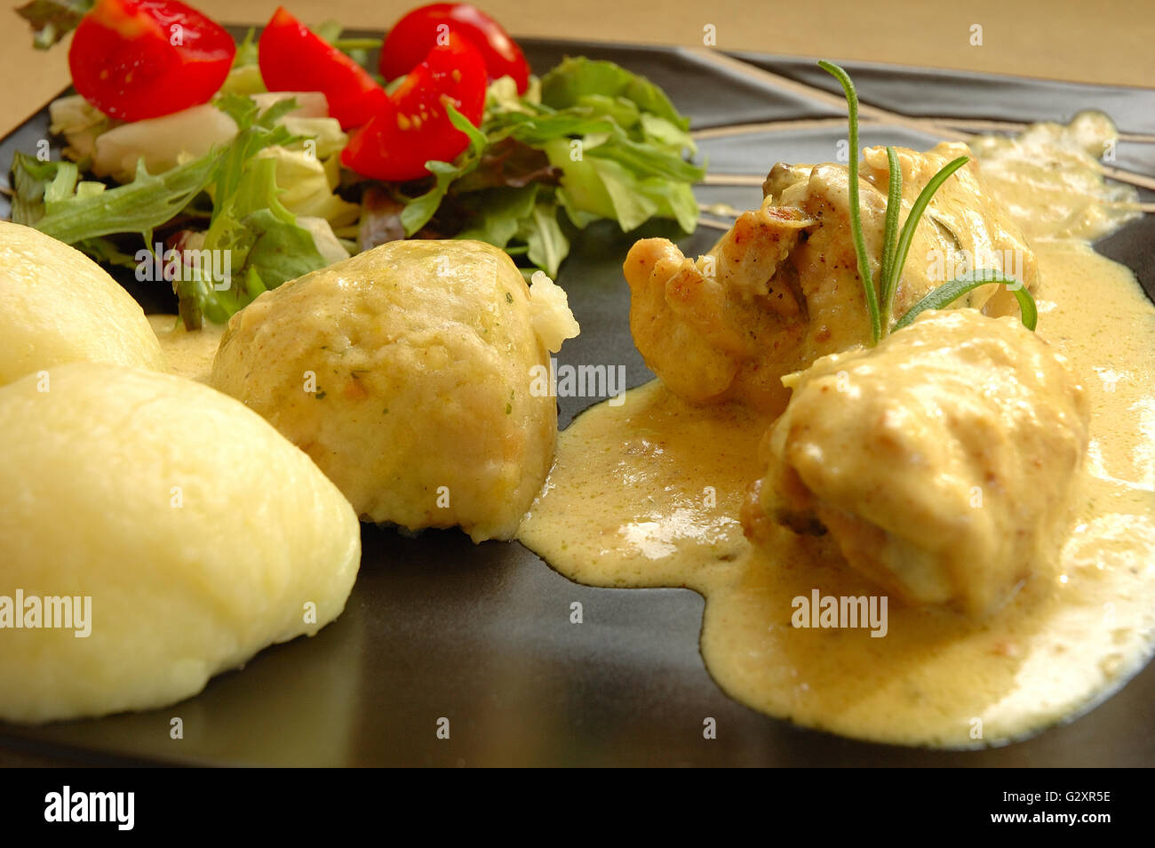 Dish consisting of rabbit meat, dumplings and salad served on black ...