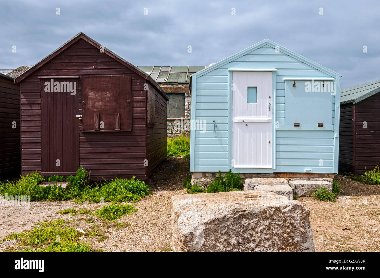 The gap between a brown and blue wooden beach hut reveals a boarded up ...