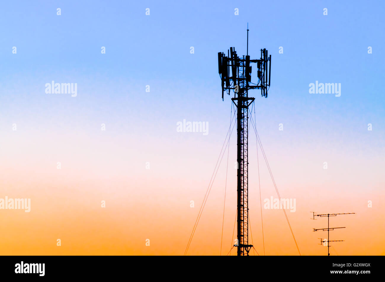 Silhouette of cellular tower against blue, pink and orange sunset sky ...