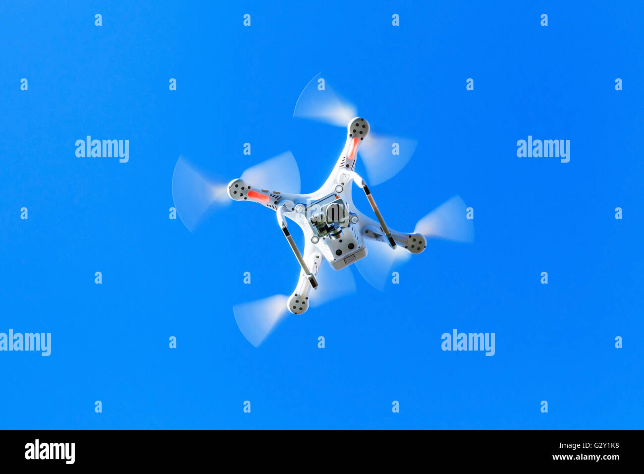White quadrocopter in blue sky, drone controlled by wireless remote ...