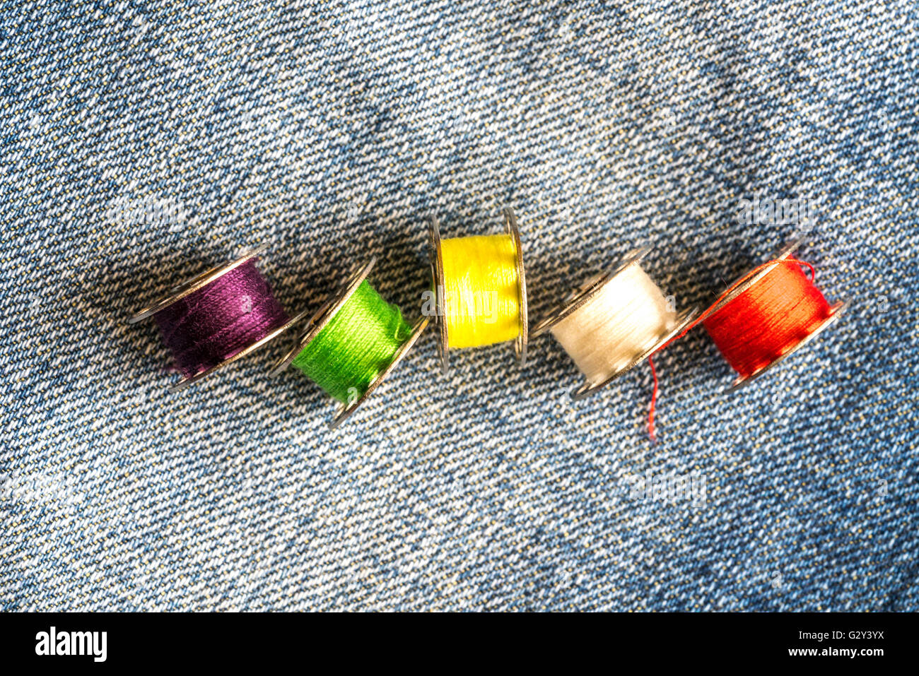 Rolls of sewing tread and blue jeans background with natural lighting ...