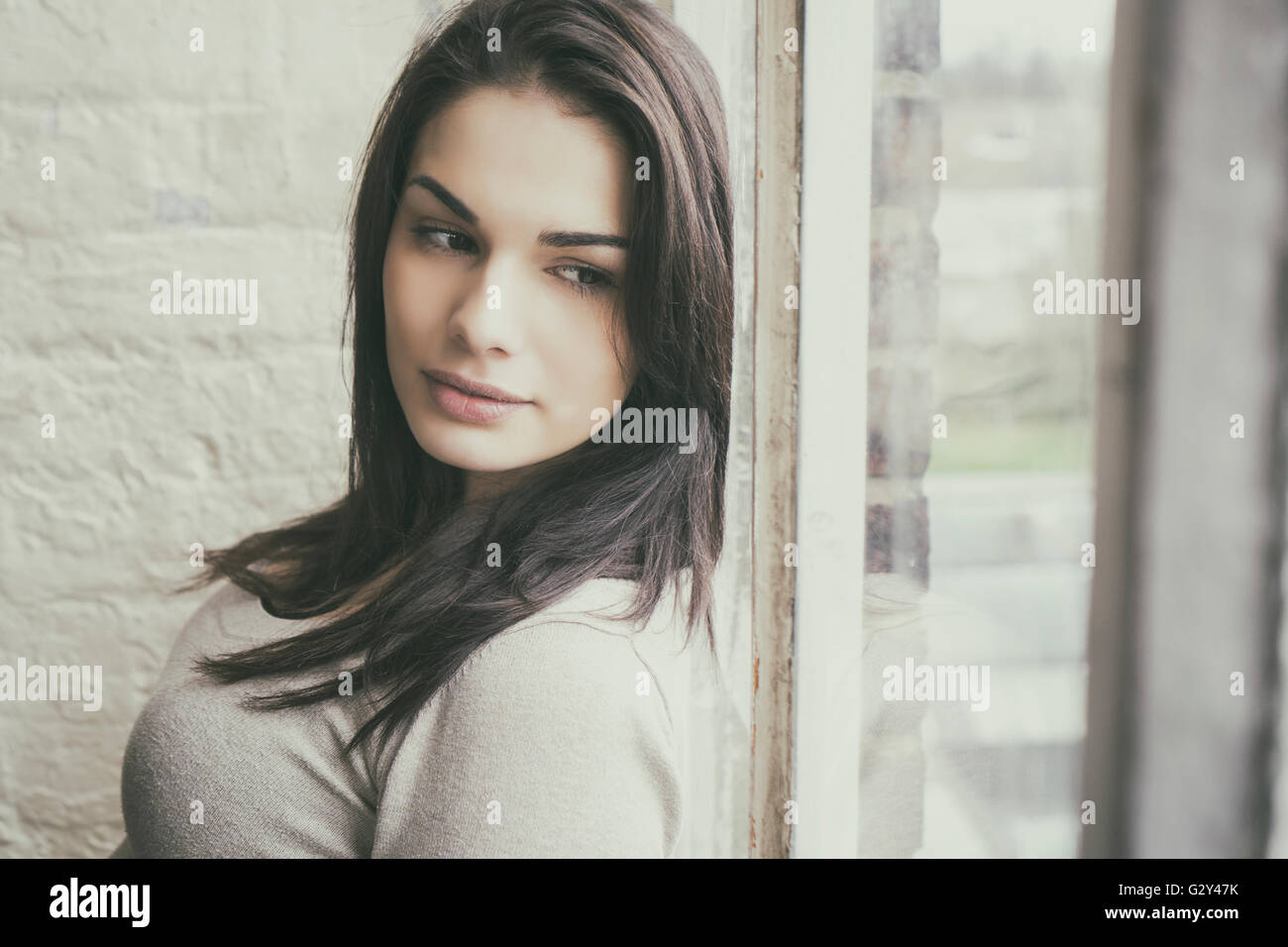 Beautiful young woman leaning against the window Stock Photo - Alamy