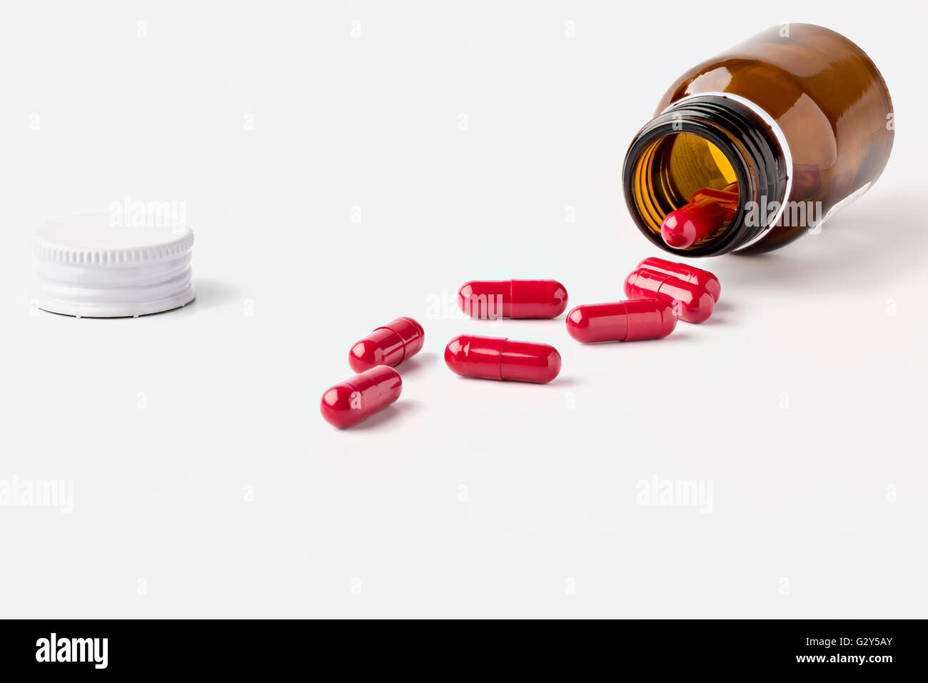 Open glass brown pill bottle and scattered red capsules on white ...