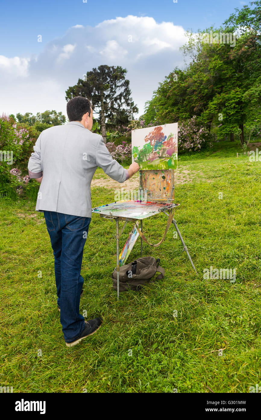 Lonely male artist working outdoors in the park or garden on a trestle ...