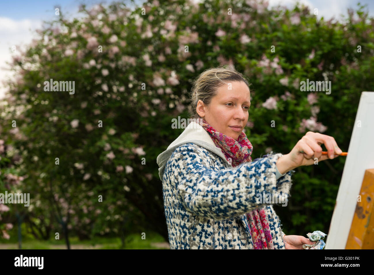 Female middle-aged contemplative artist working on a trestle and easel ...