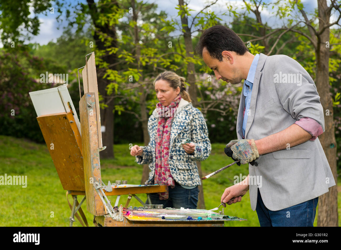 Two middle-aged dreamy artists working on a trestle and easel painting ...