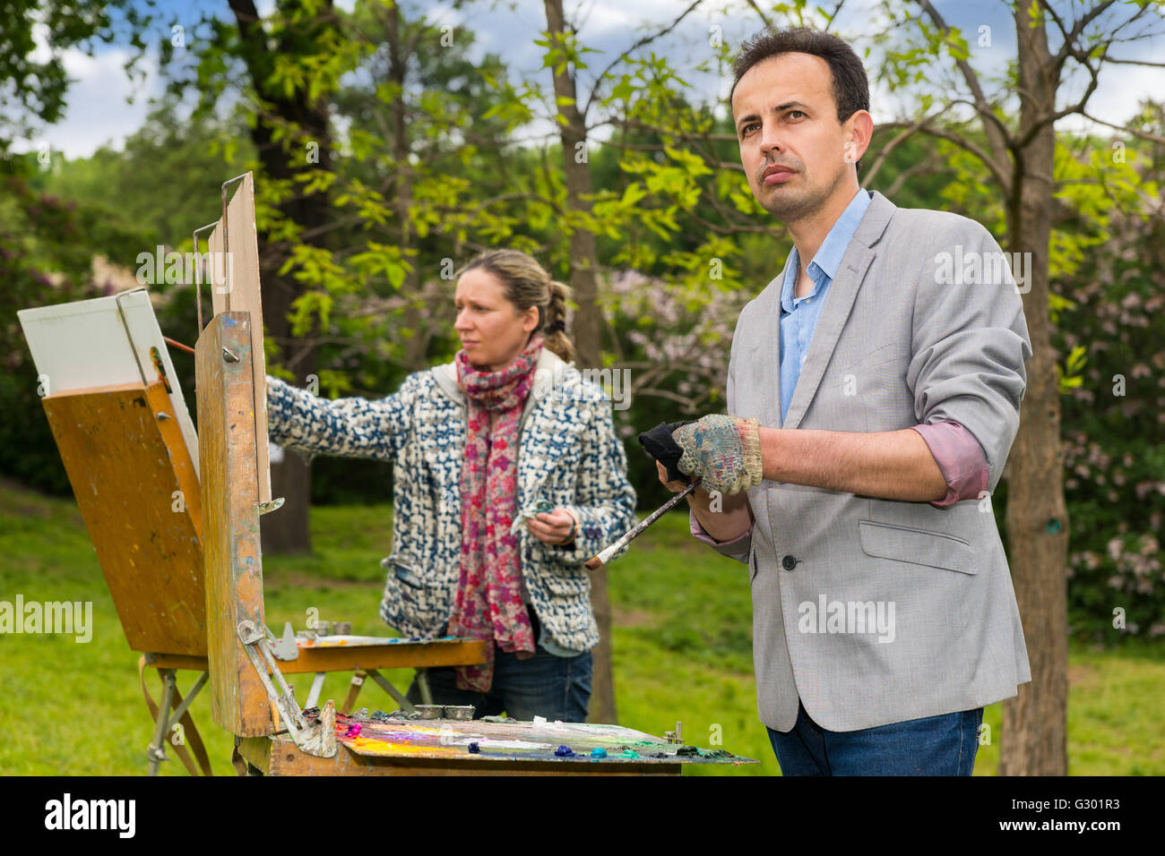 Two middle-aged dreamy painters working on a trestle and easel painting ...
