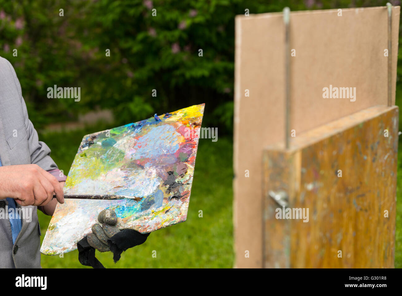 Artist holding a colorful palette and a paintbrush mixing colors in ...