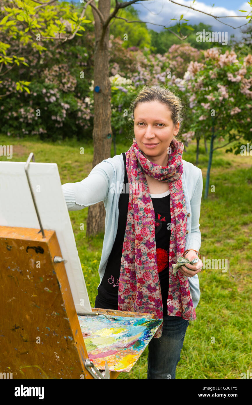 Cheerful female painter working working on a trestle and easel painting ...