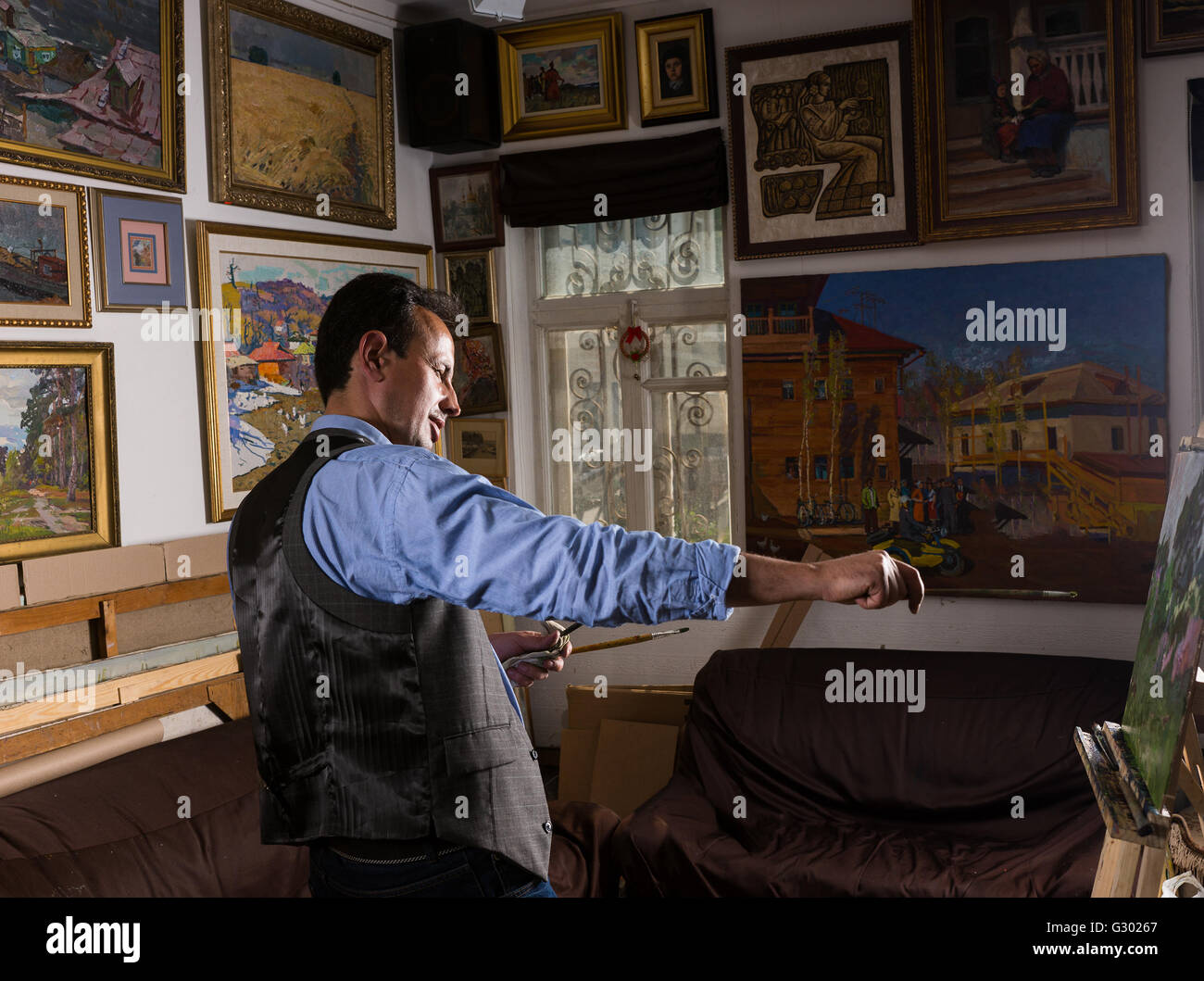 Handsome painter evaluating his masterpiece holding paintbrushes and ...