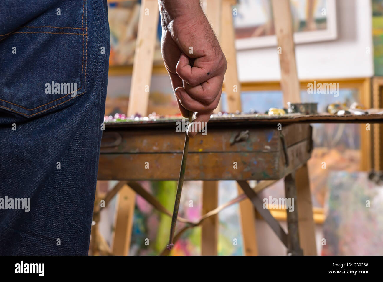 Male artist hand holding a tiny paintbrush standing in a gallery or art ...