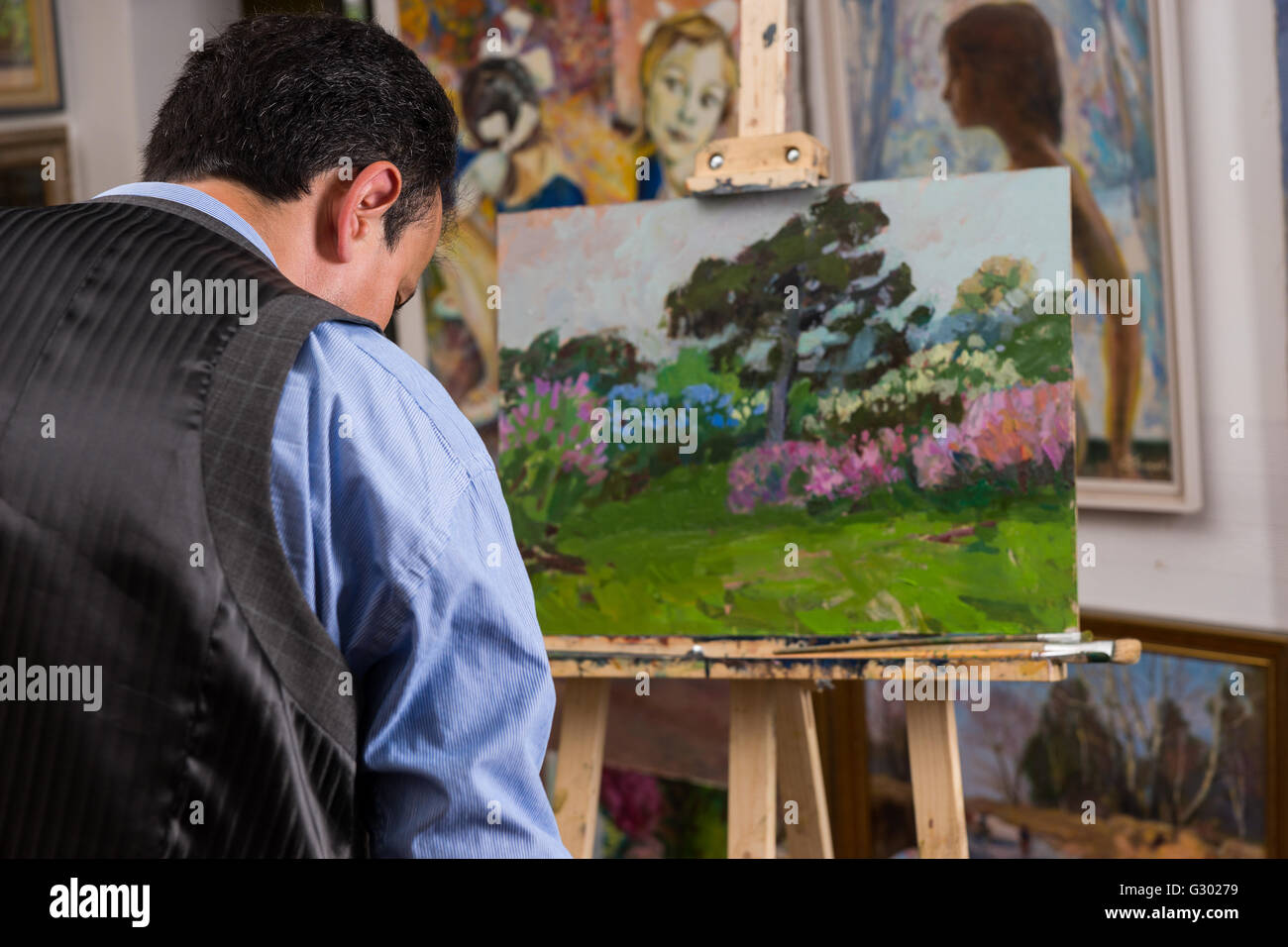 Painter working on a masterpiece in his gallery painting a garden scene ...