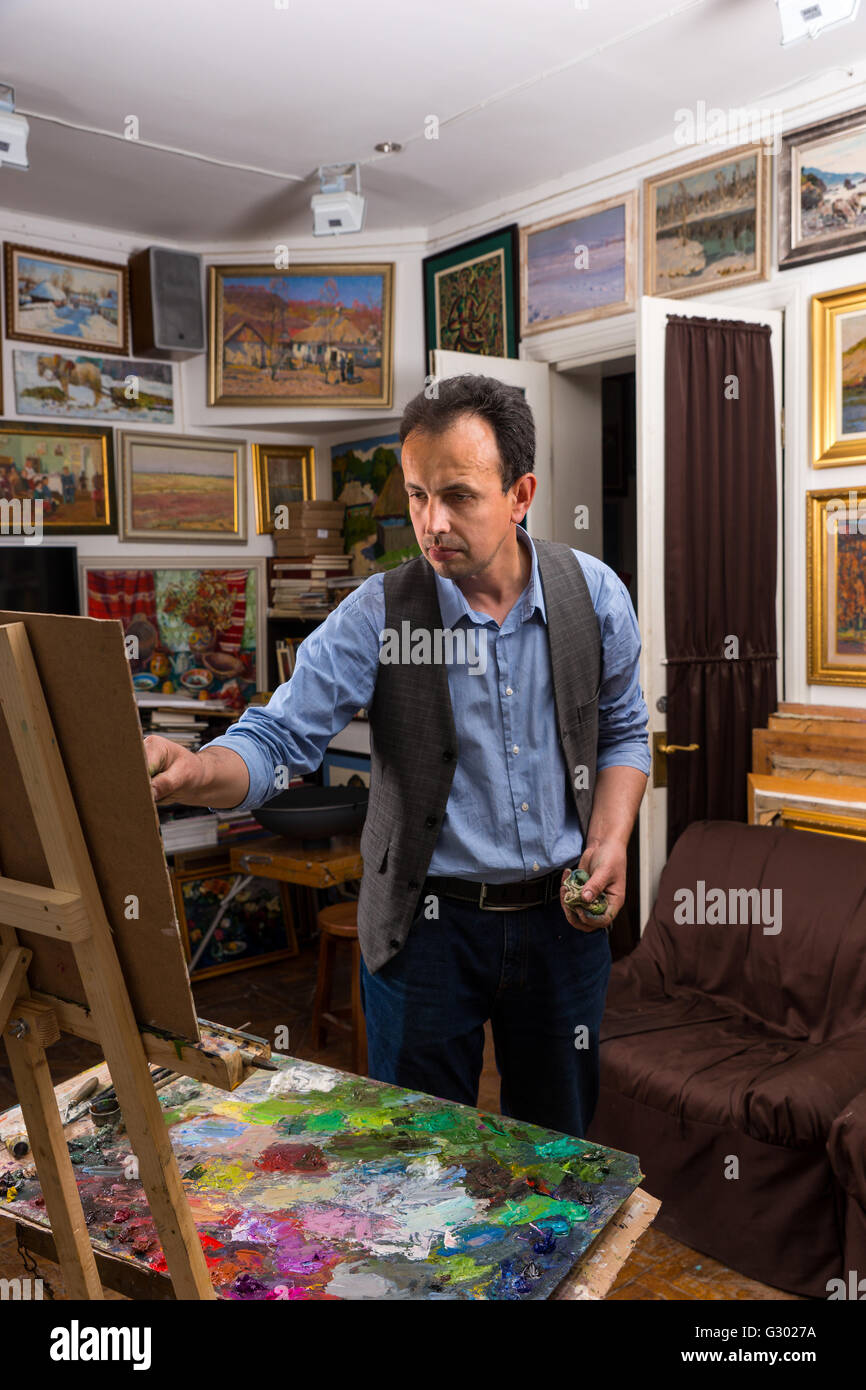Handsome artist in the process of painting his masterpiece in his ...