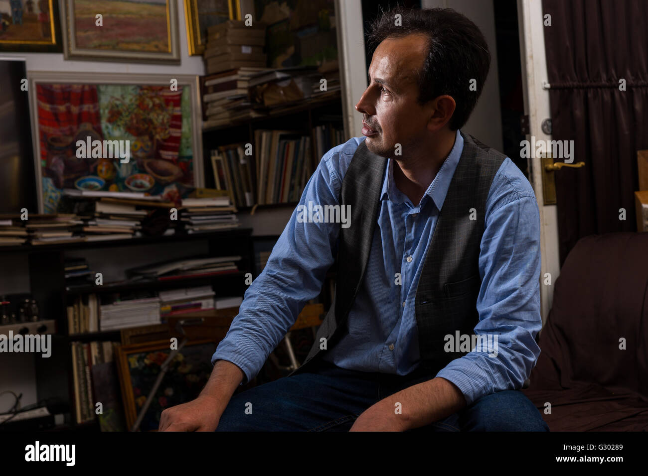 Portrait of male artist sitting looking trough his studio with a paint ...