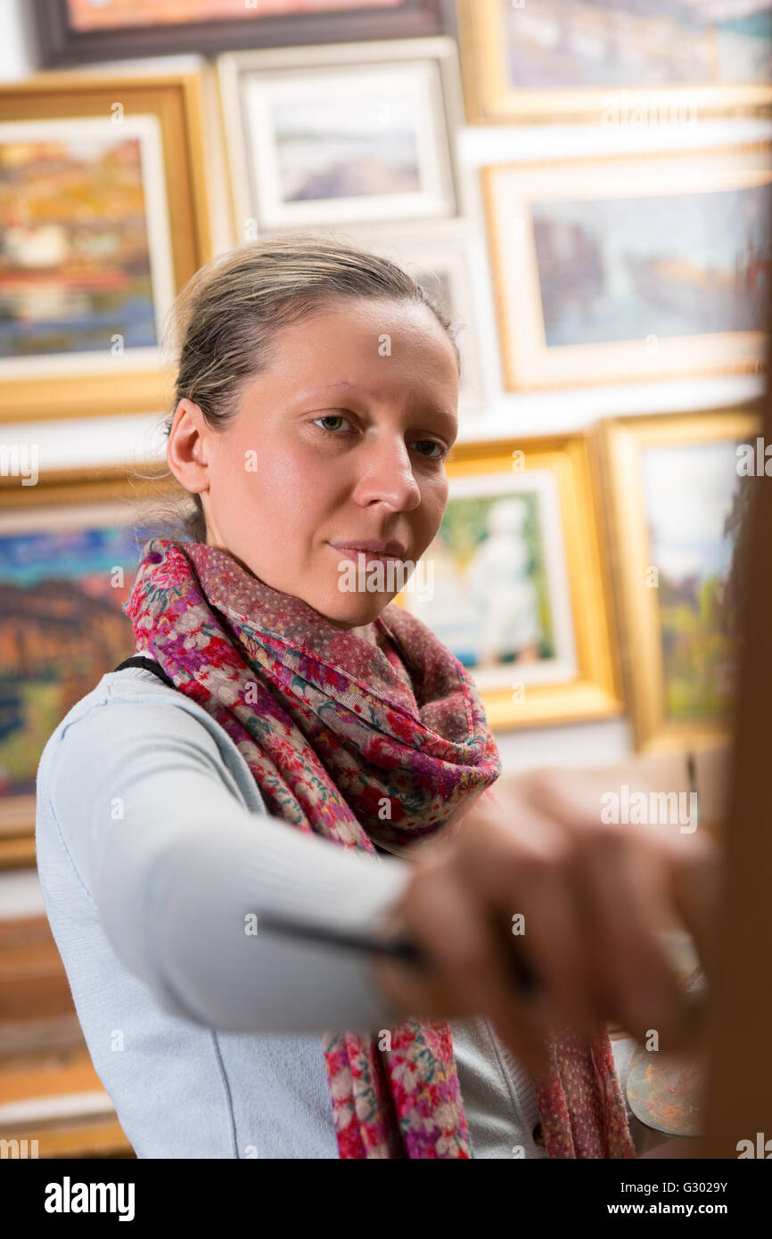 Portrait of female painter working on a canvas on an easel in a studio ...