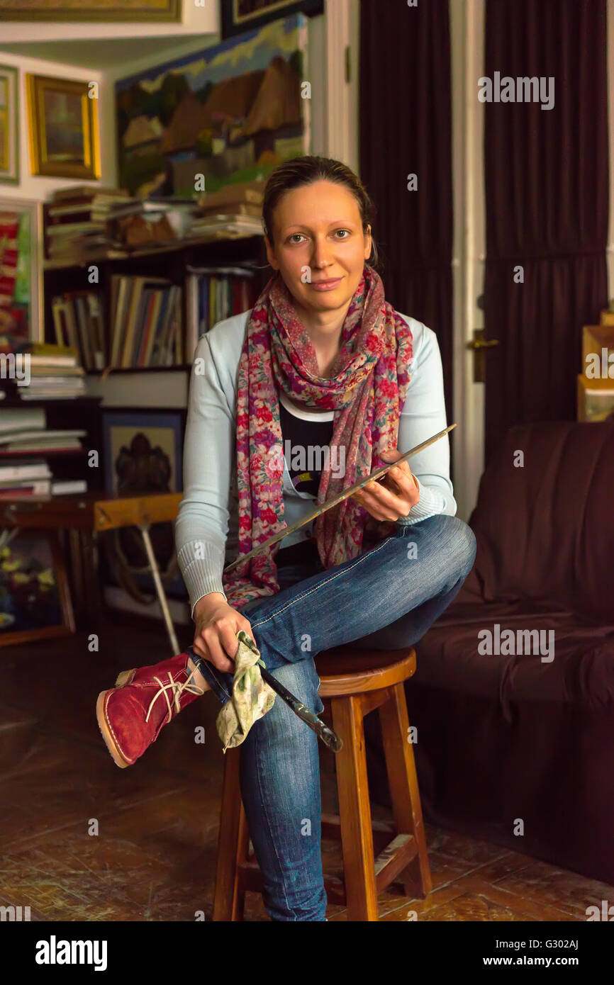 Beautiful painter sitting painting in a studio or gallery holding a ...