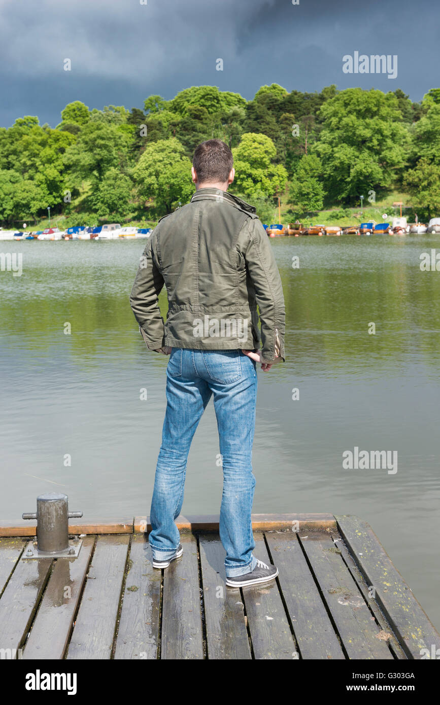 Man standing on jetty by a lake and looking at rainclouds Stock Photo ...