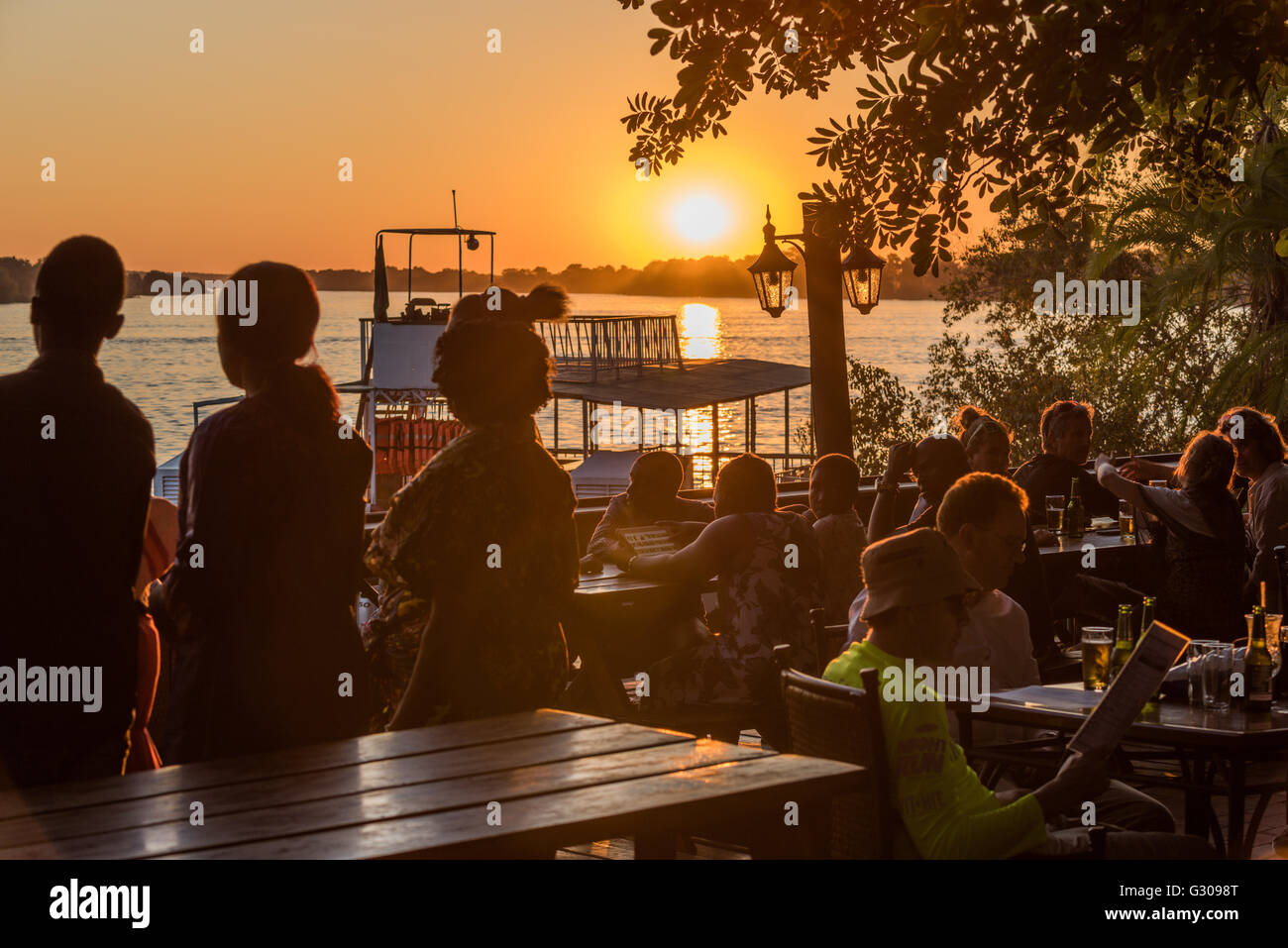 People drinking at tables watching sun set Stock Photo - Alamy