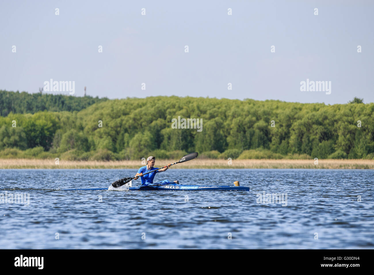 young man athlete on rowing kayak on lake during Ural championship in ...
